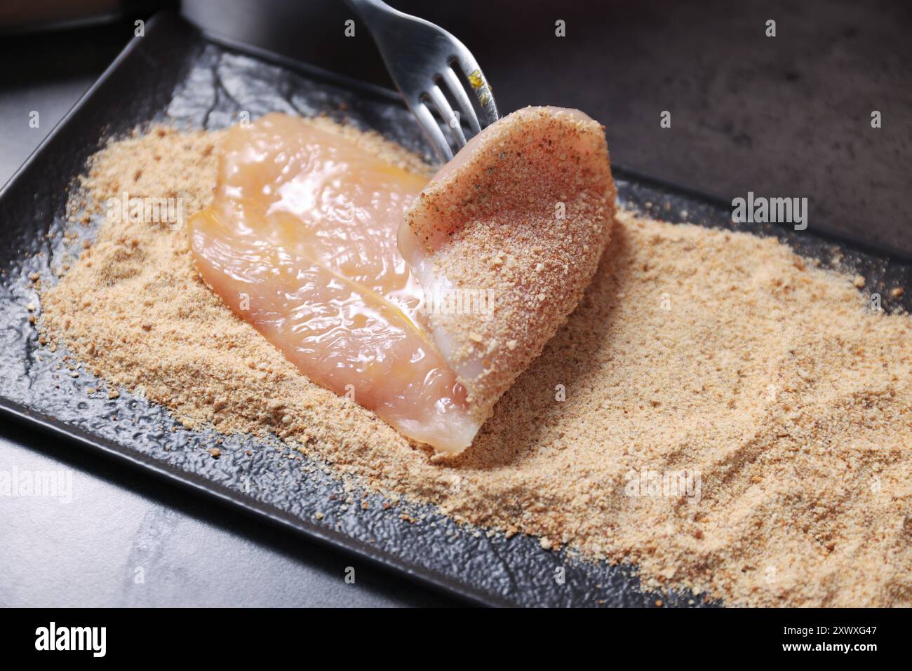 Making schnitzel. Coating slice of meat with bread crumbs at dark table ...