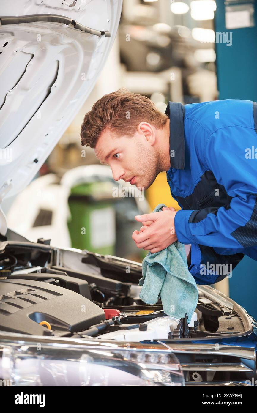 Mechanic examining car. Confident young man in uniform examining car ...