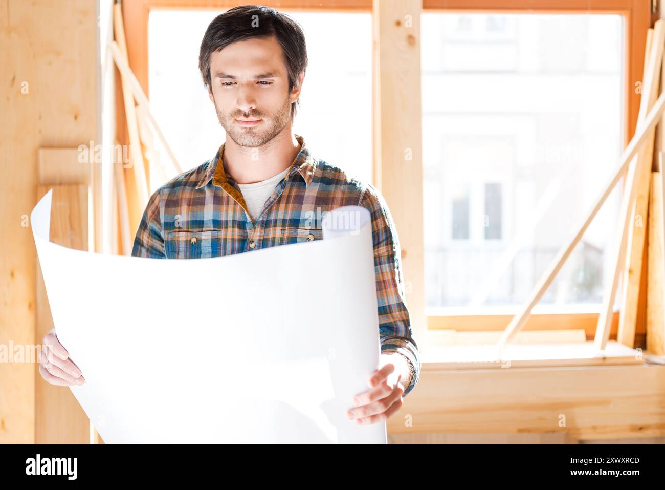 Reviewing the plan. Confident young man looking through blueprint while ...