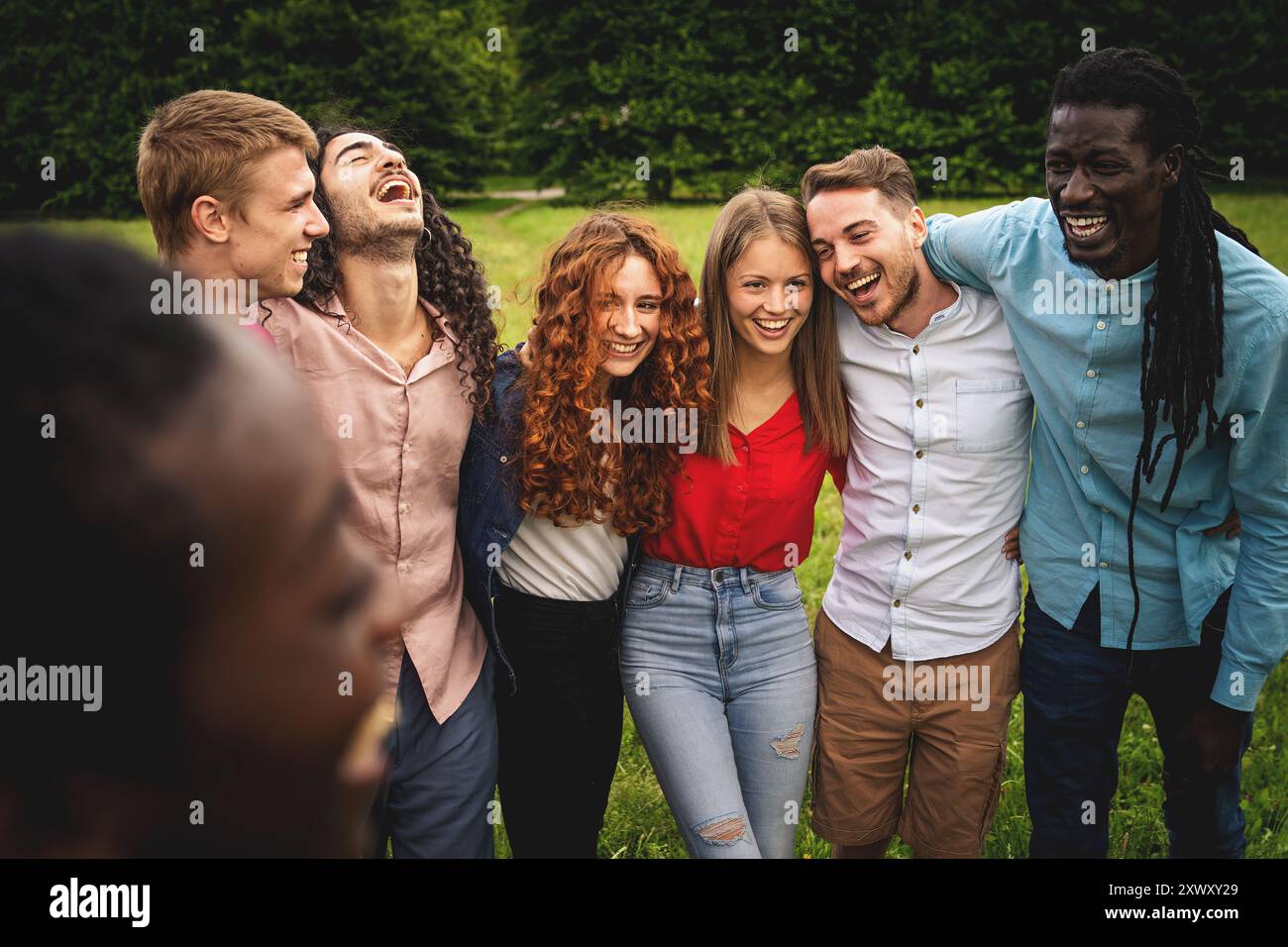 Joyful diverse group of young friends laughing and embracing in a park ...