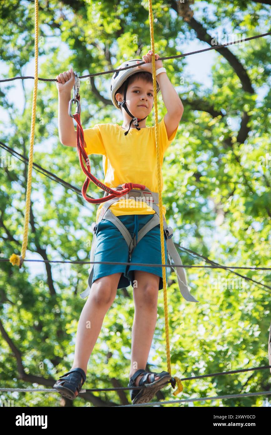 Child in helmet climbing in rope park, walking on ropeway overcoming ...