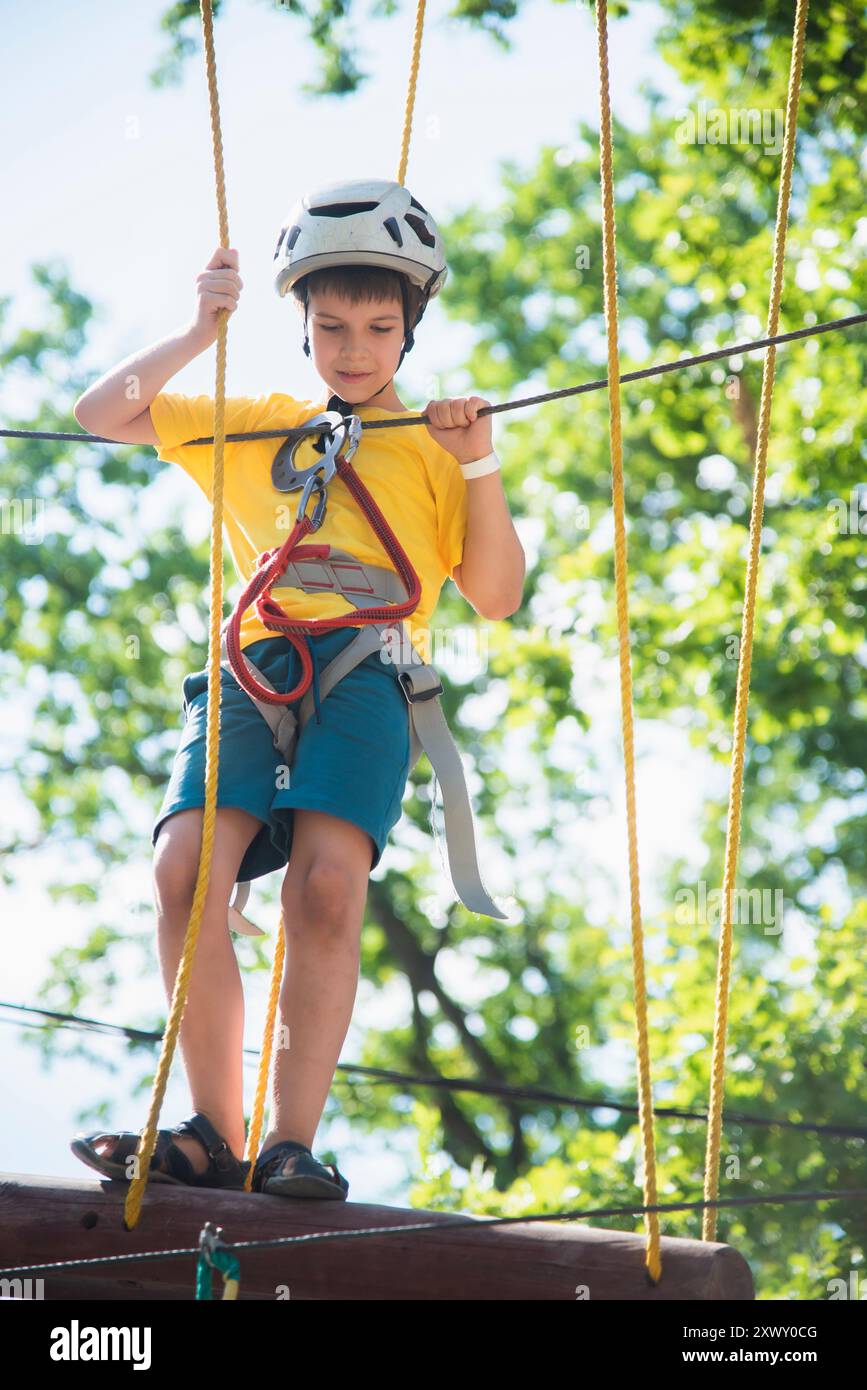 A boy is rock climbing in a rope park, walking along a cable car and ...