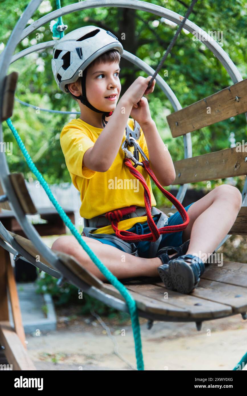 Child in helmet climbing in rope park, walking on ropeway overcoming ...