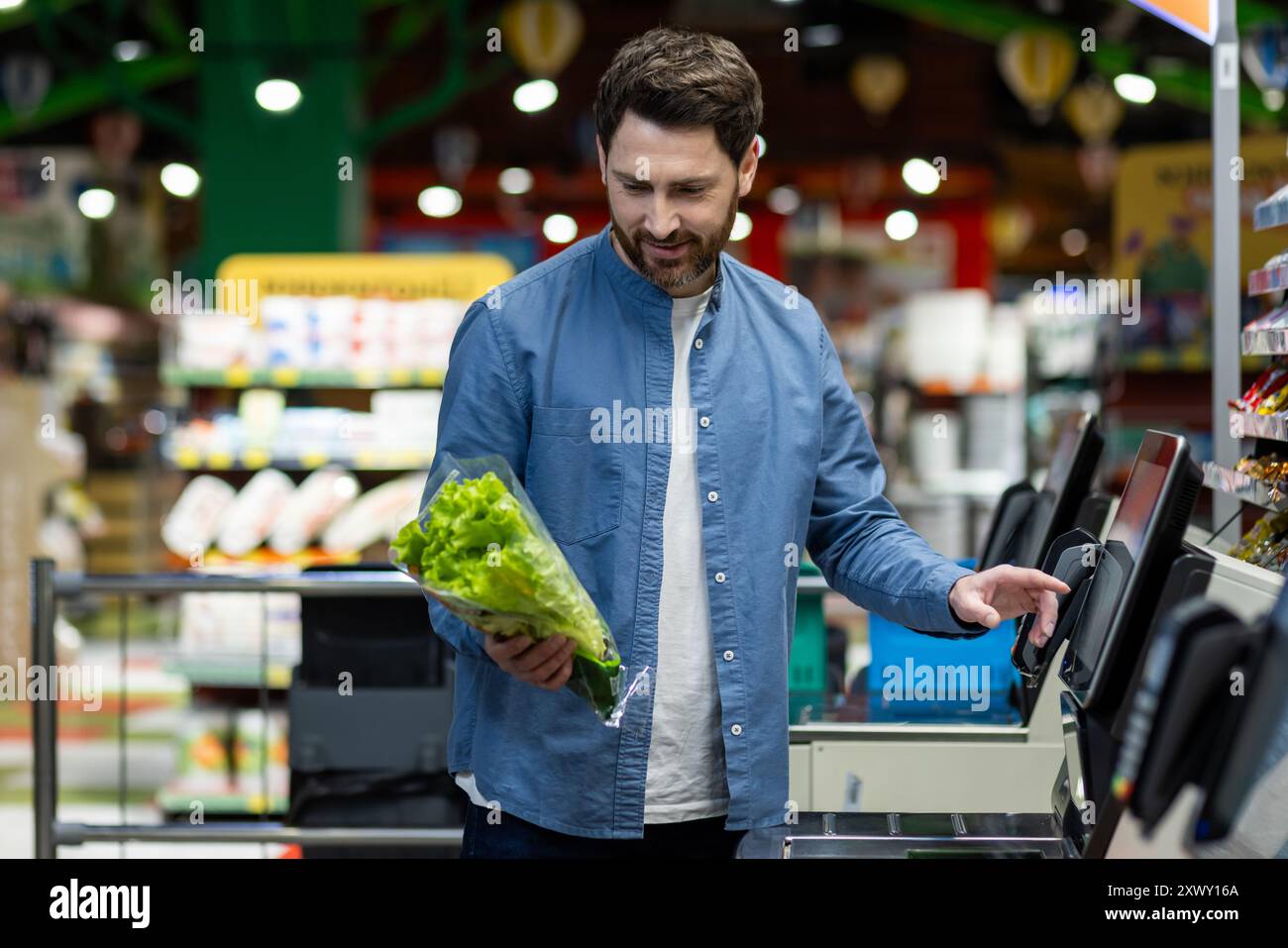 Man using self-checkout machine in grocery store, holding fresh lettuce ...