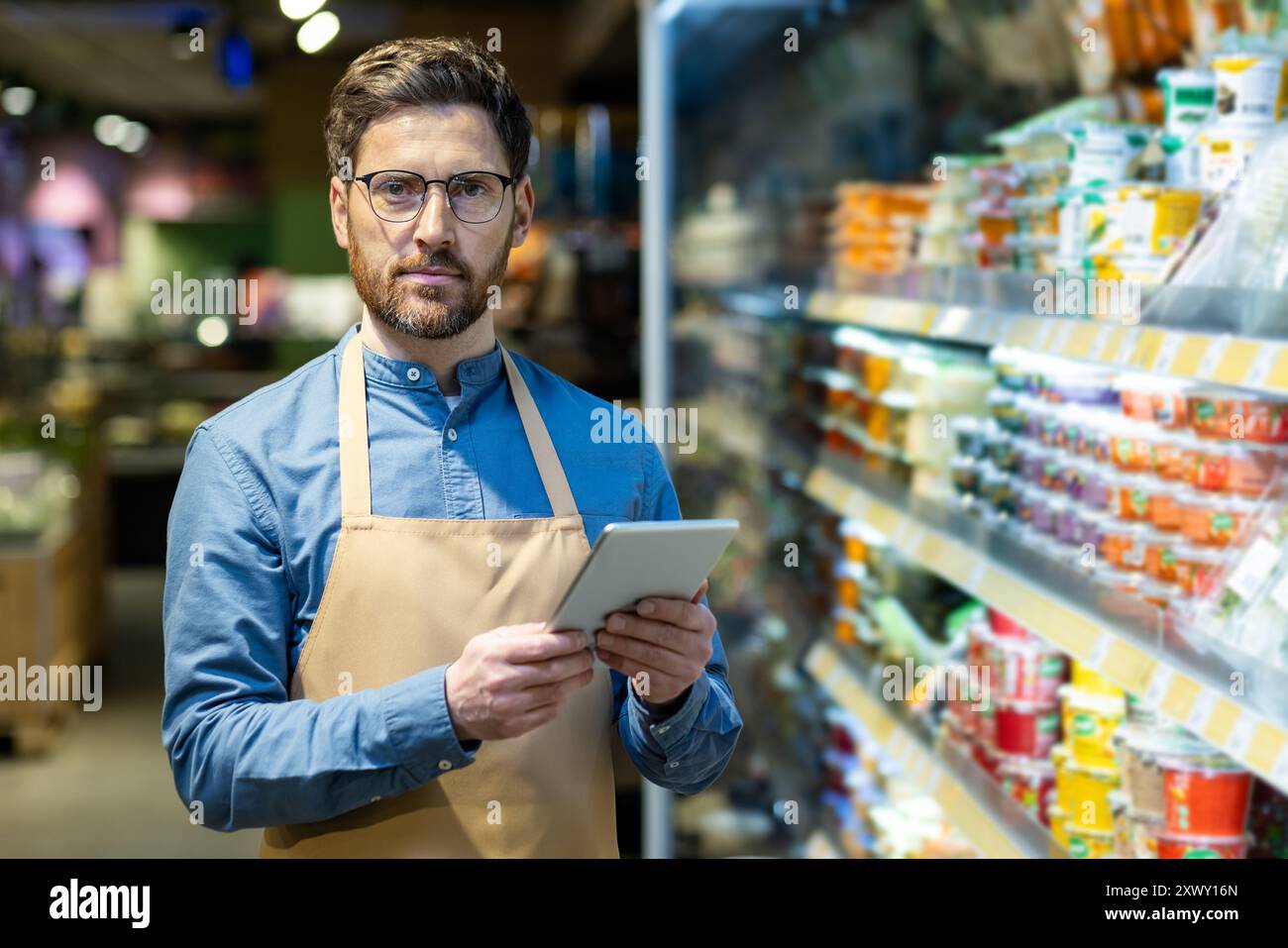 Supermarket worker standing in grocery aisle with tablet, dressed in ...