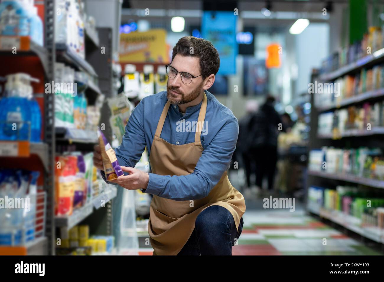 Store employee kneeling in supermarket aisle arranging products. Man ...