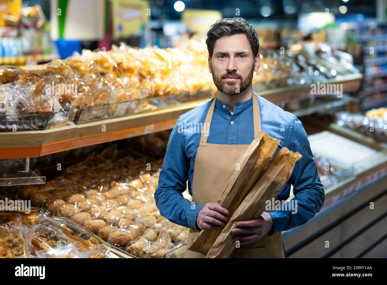 Baker with aprons holds fresh baguettes in bakery shop. Shelves display ...