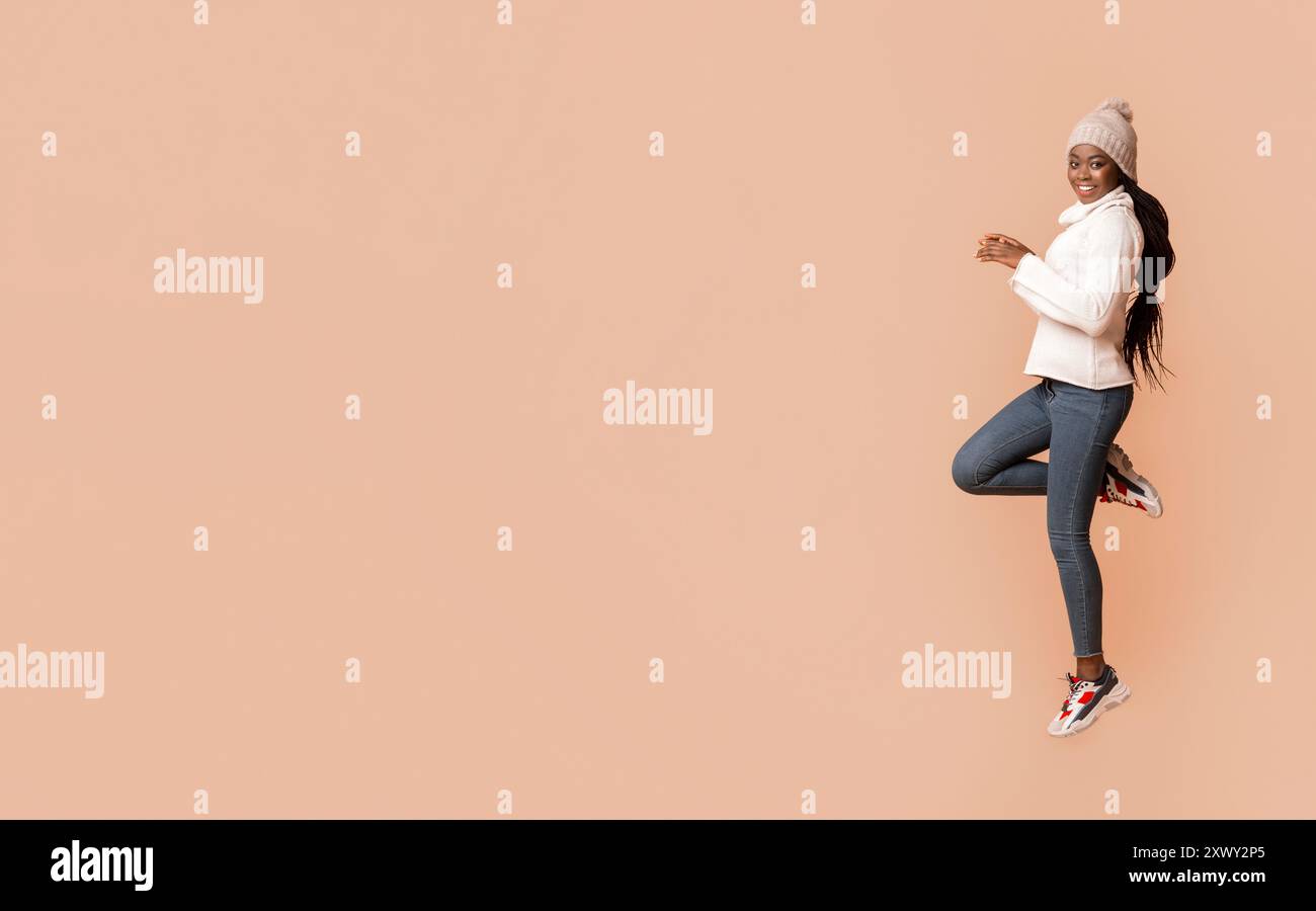 Sporty winter woman jumping on one leg over beige background Stock ...