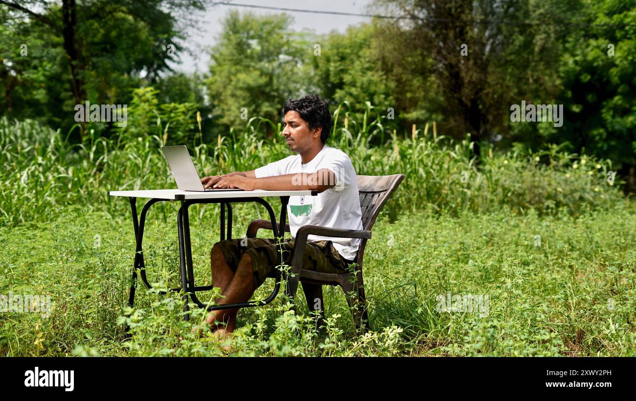 Indian young boy using laptop at outdoor. Man sitting with office table ...