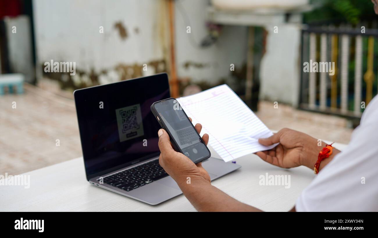 Young Indian man paying bills using mobile and laptop. QR code scan and ...