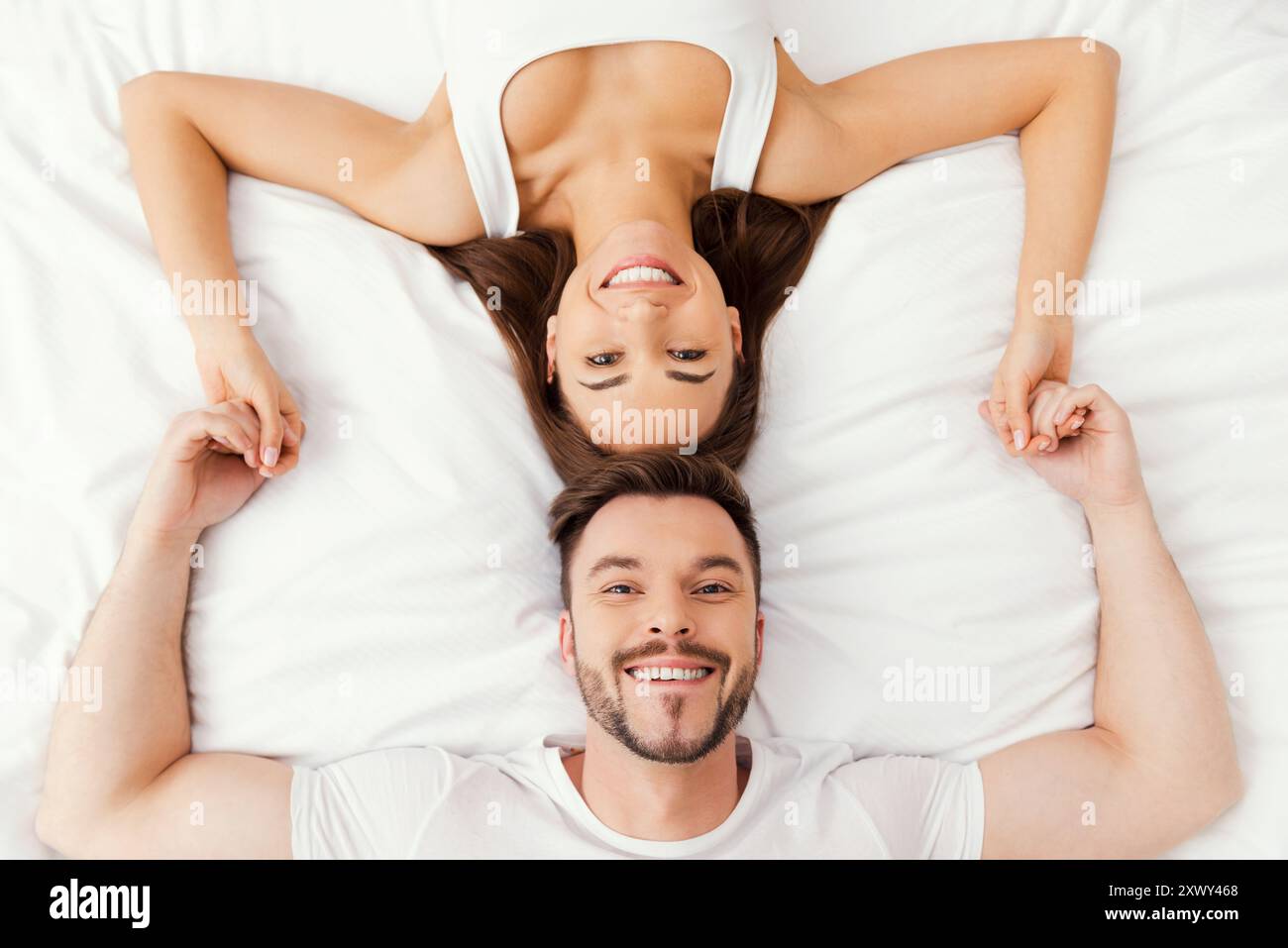 Relaxing in bed together. Top view of beautiful young loving couple lying in bed together and ...