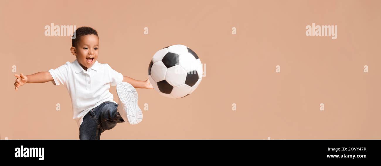 Adorable little boy playing football, hitting ball over yellow ...