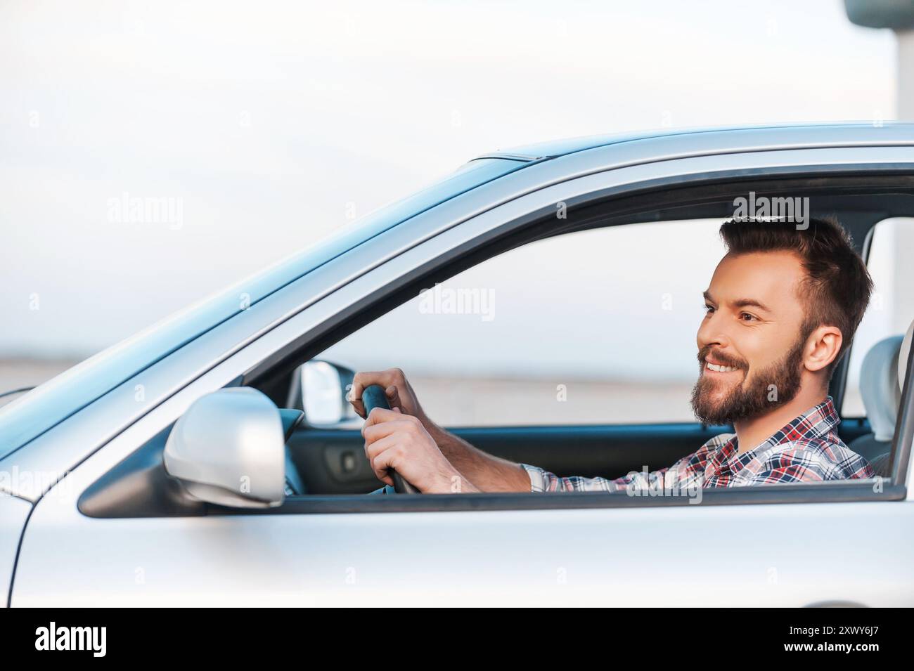 Riding his new car. Side view of handsome young man driving his car and ...