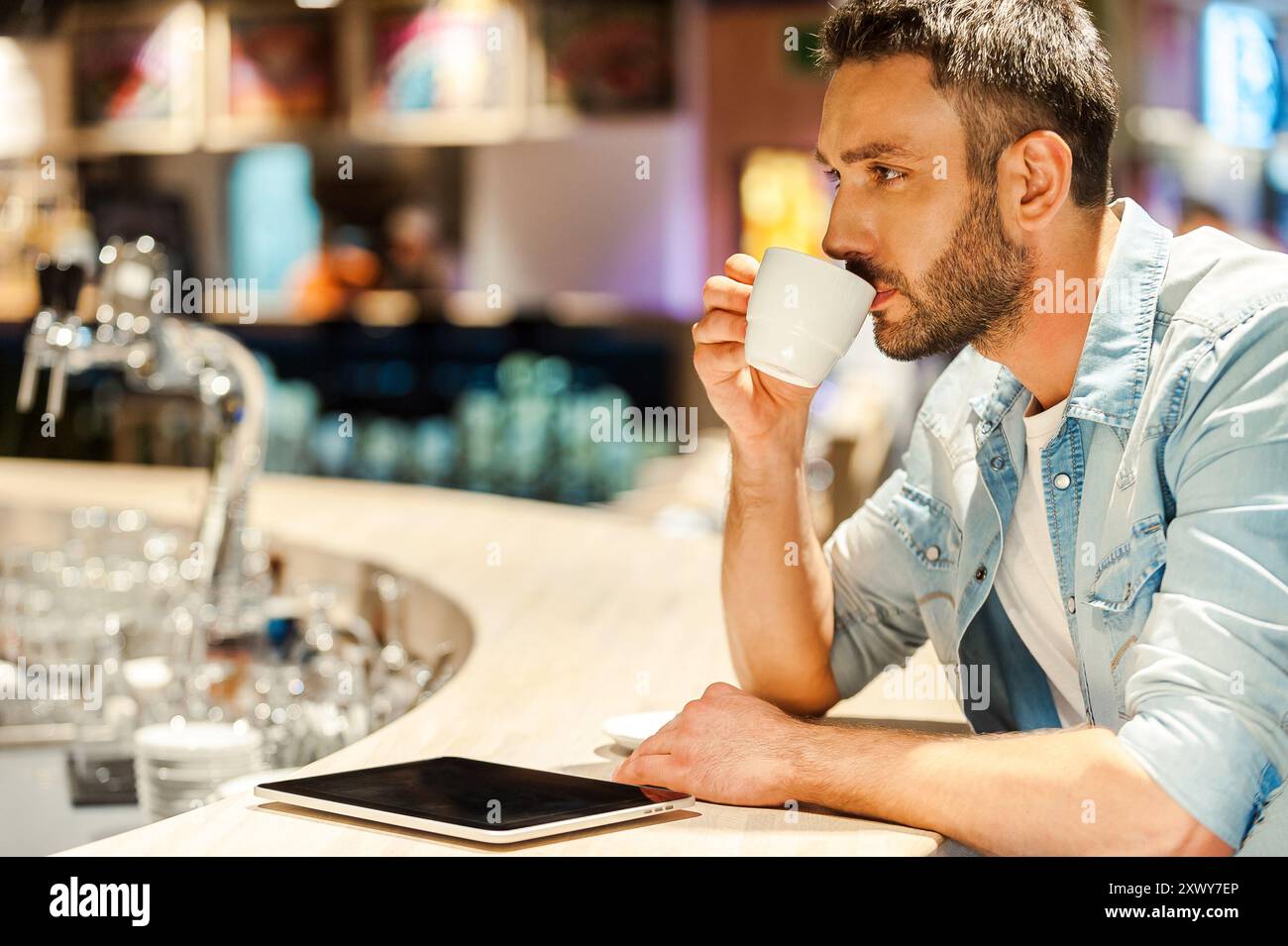Coffee break. Side view of young man drinking coffee while sitting at ...