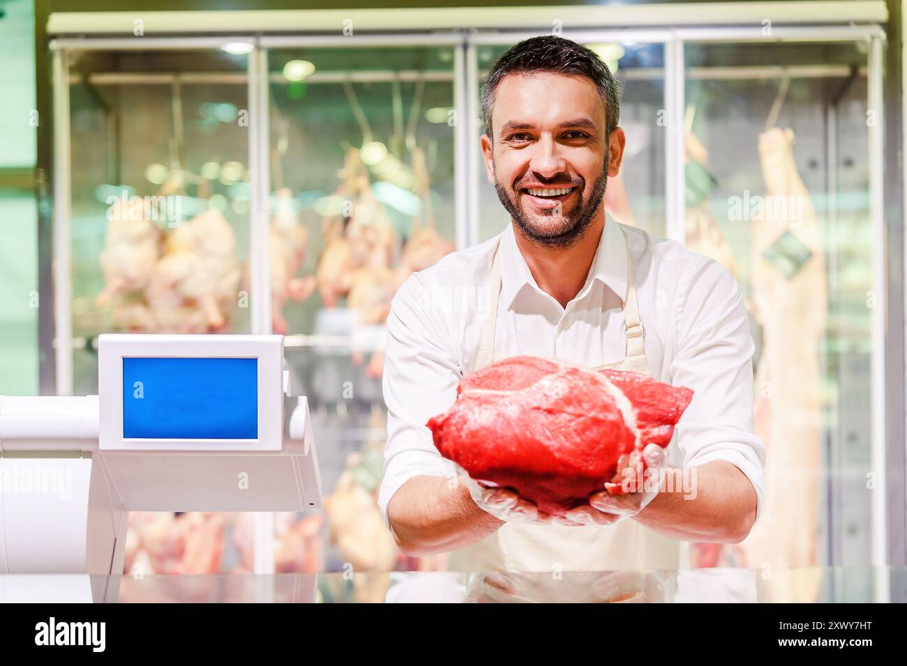 The best quality meat for you. Cheerful young butcher stretching out ...