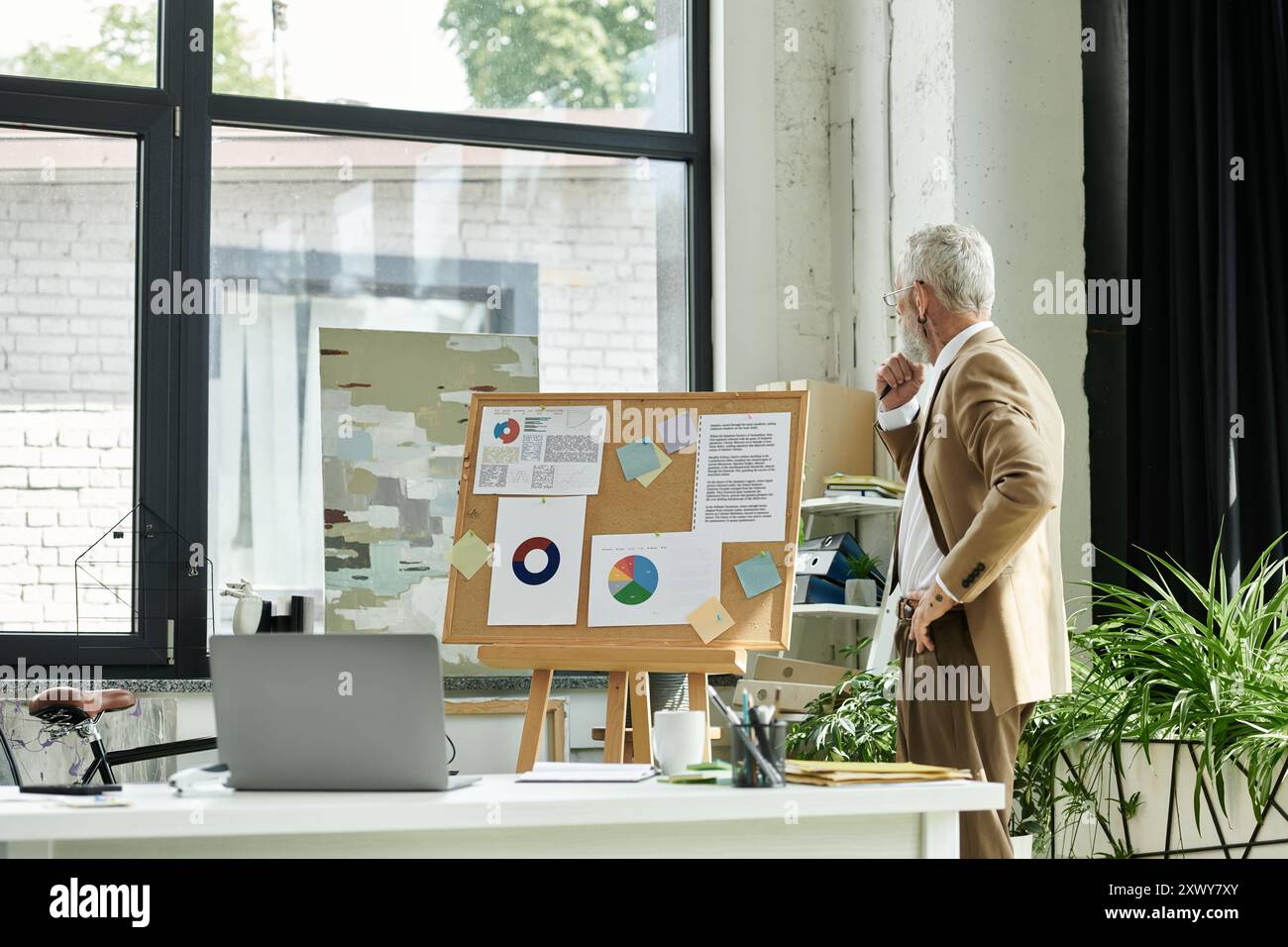 Middle-aged man in brown suit in home office, by window, looking at ...