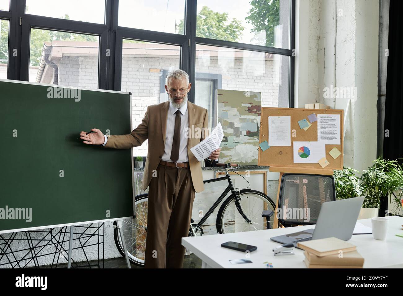A bearded teacher gestures at a whiteboard in a modern classroom ...