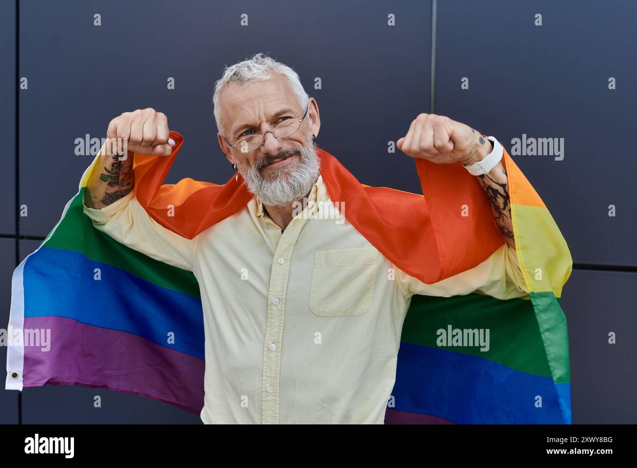 A smiling, mature man with a beard stands proudly with a rainbow flag ...