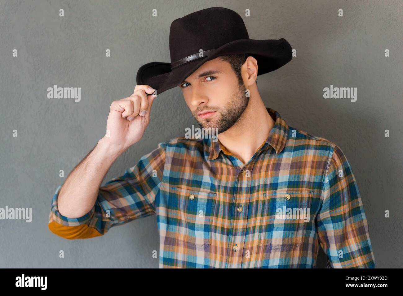 Cowboy style. Handsome young man adjusting his cowboy hat and looking ...