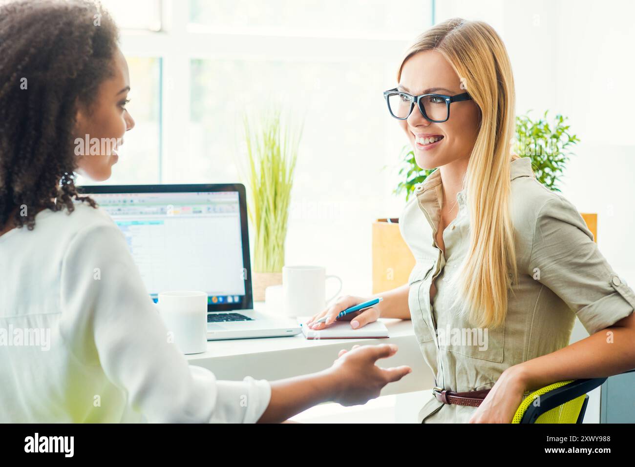 Discussing work together. Two happy young women discussing something ...