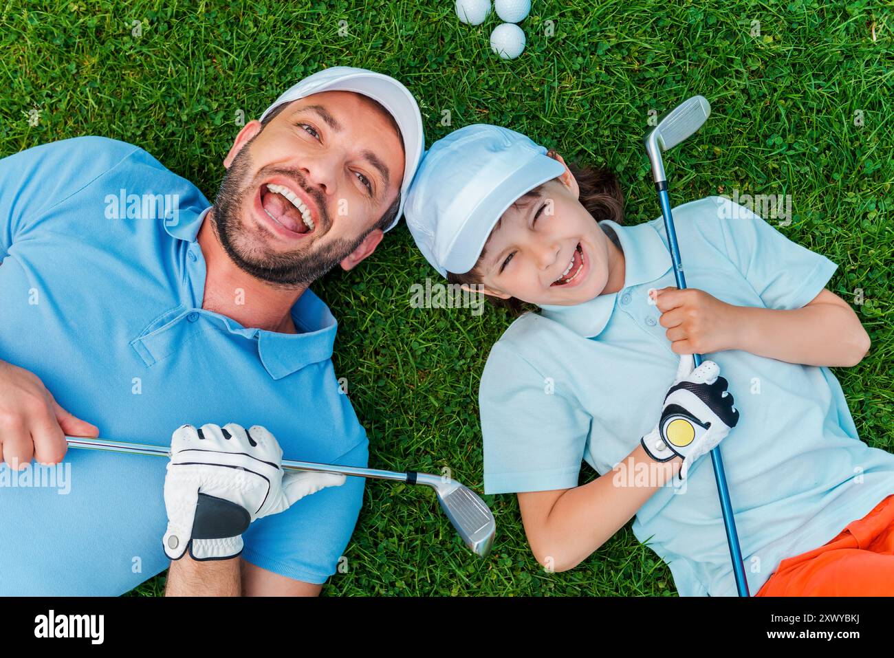 Happy golfers. Top view of cheerful little boy and his father holding golf clubs and smiling ...