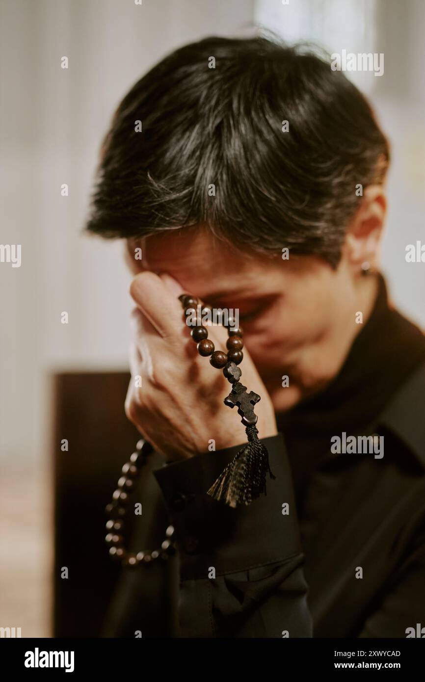 Medium close up of mournful woman squeezing wooden rosary and putting ...