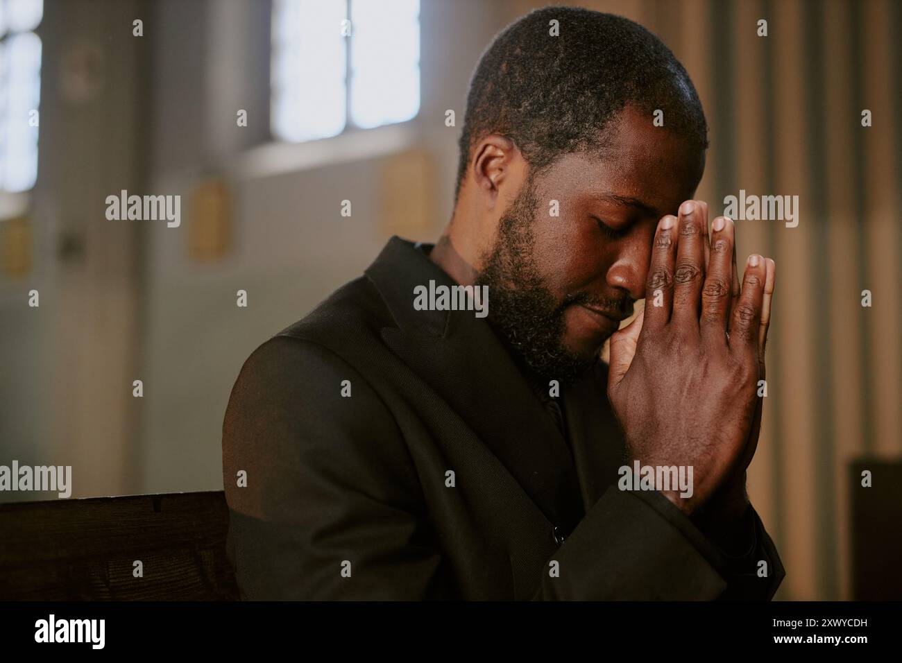 African American Man sitting on wooden bench and praying to God during ...