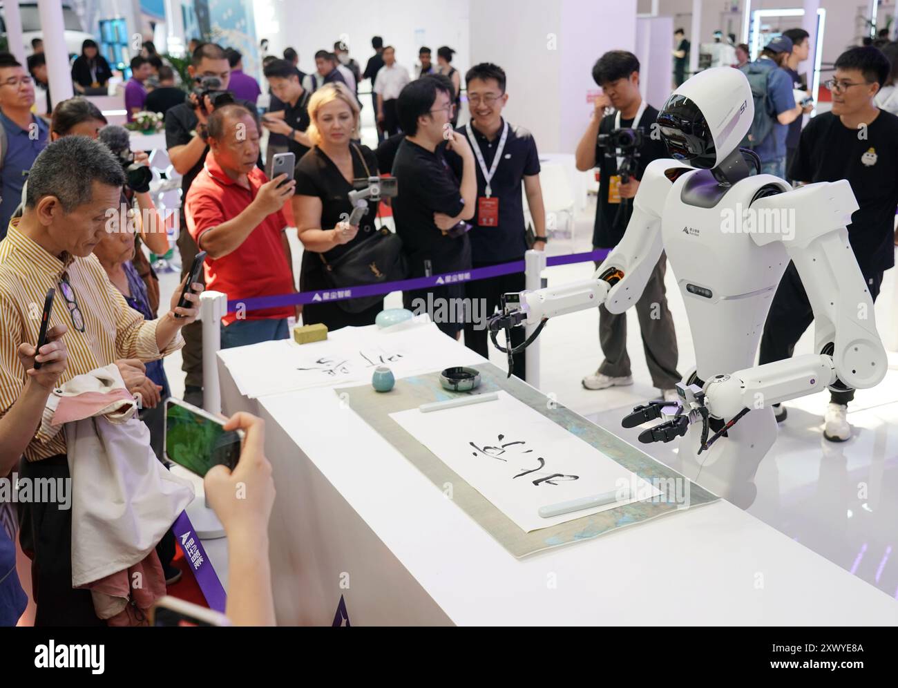 Beijing, China. 21st Aug, 2024. Visitors watch as a robot writes ...