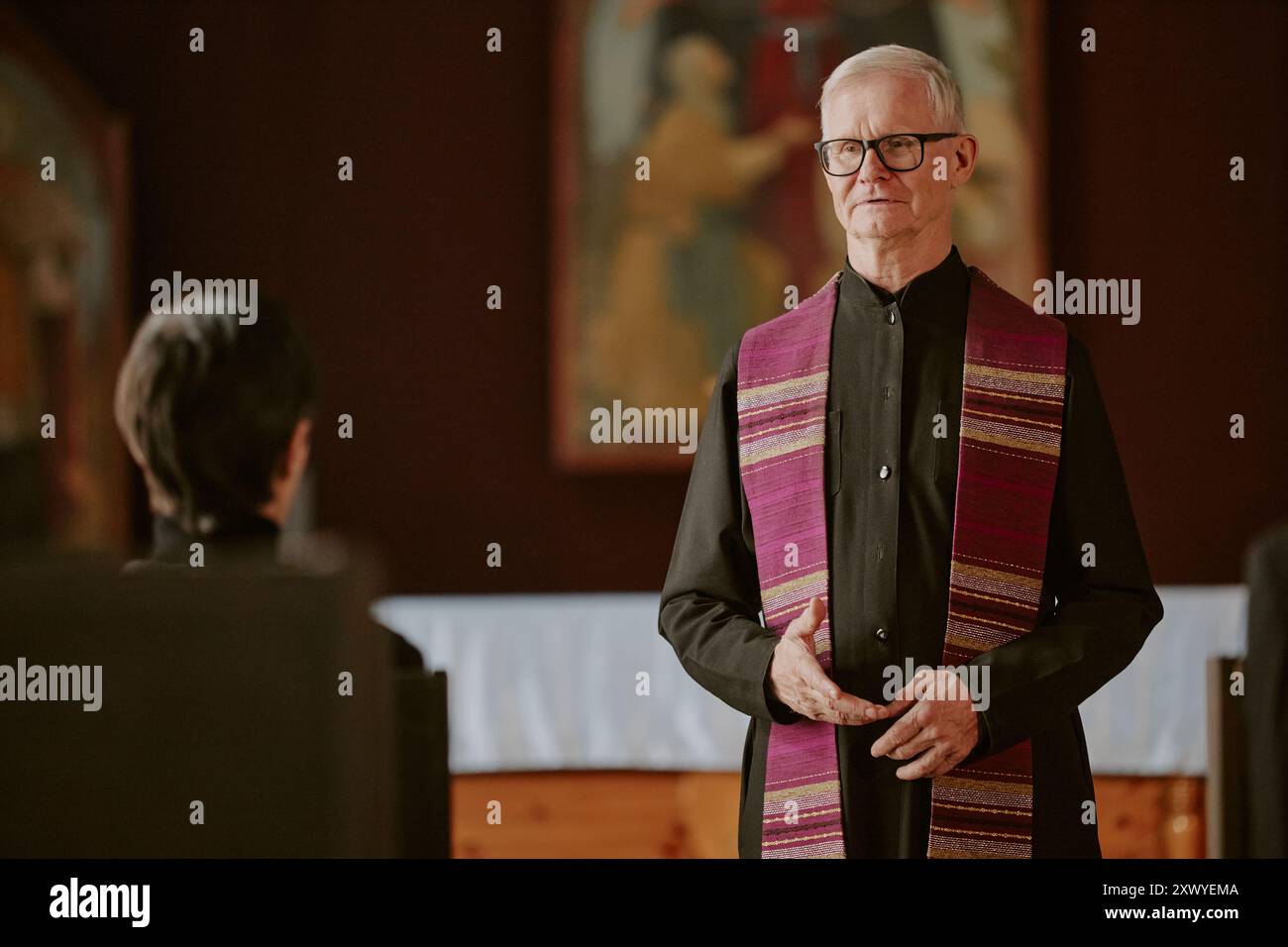 Silver-haired pastor dressed in black robe saying prayer during funeral ...
