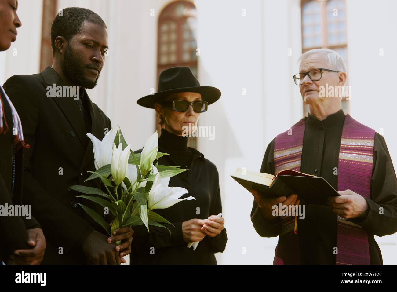 Senior priest reading prayer during funeral while biracial family ...