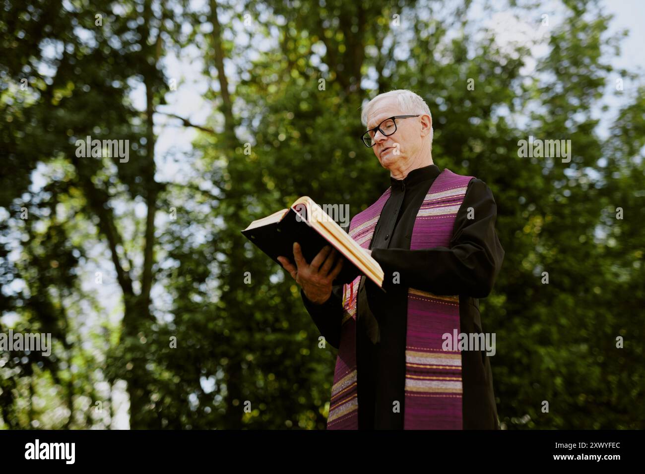 Low angle shot of senior priest in black vestment holding Bible and ...