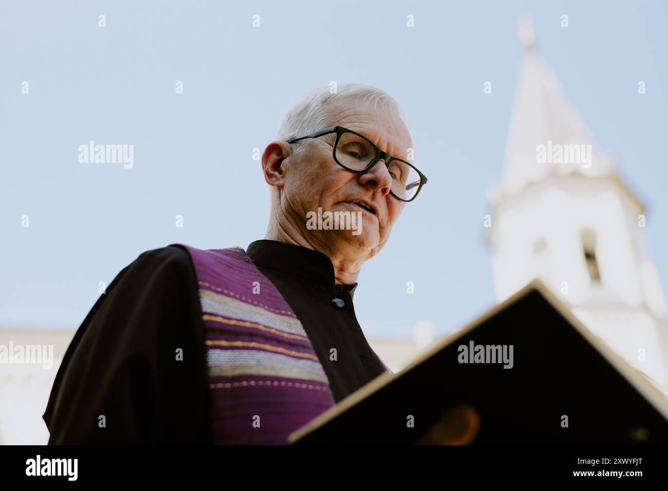 Low angle shot of senior Caucasian pastor reading Bible at funeral ...