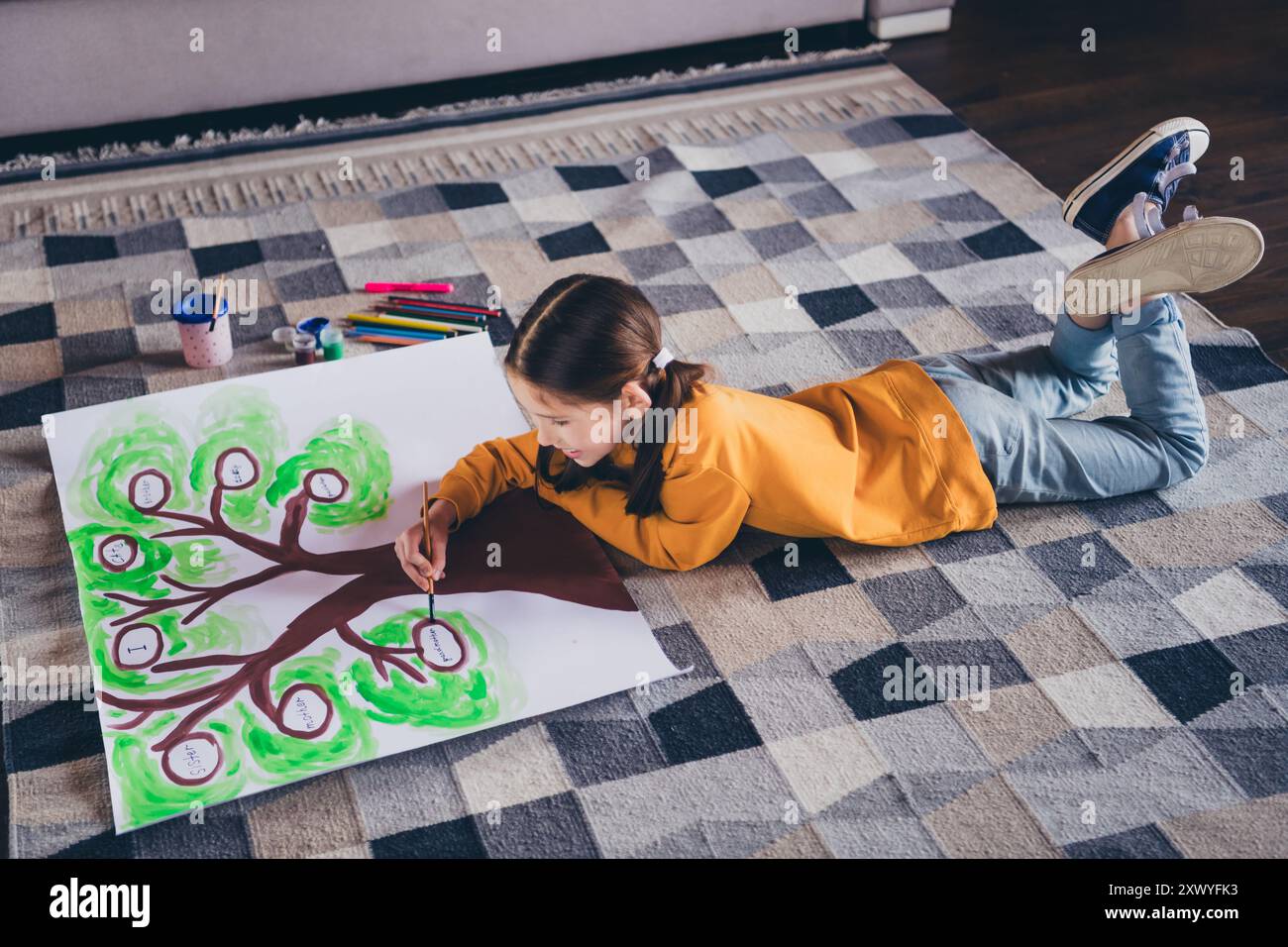 Full body photo of nice little girl lying floor drawing family tree ...