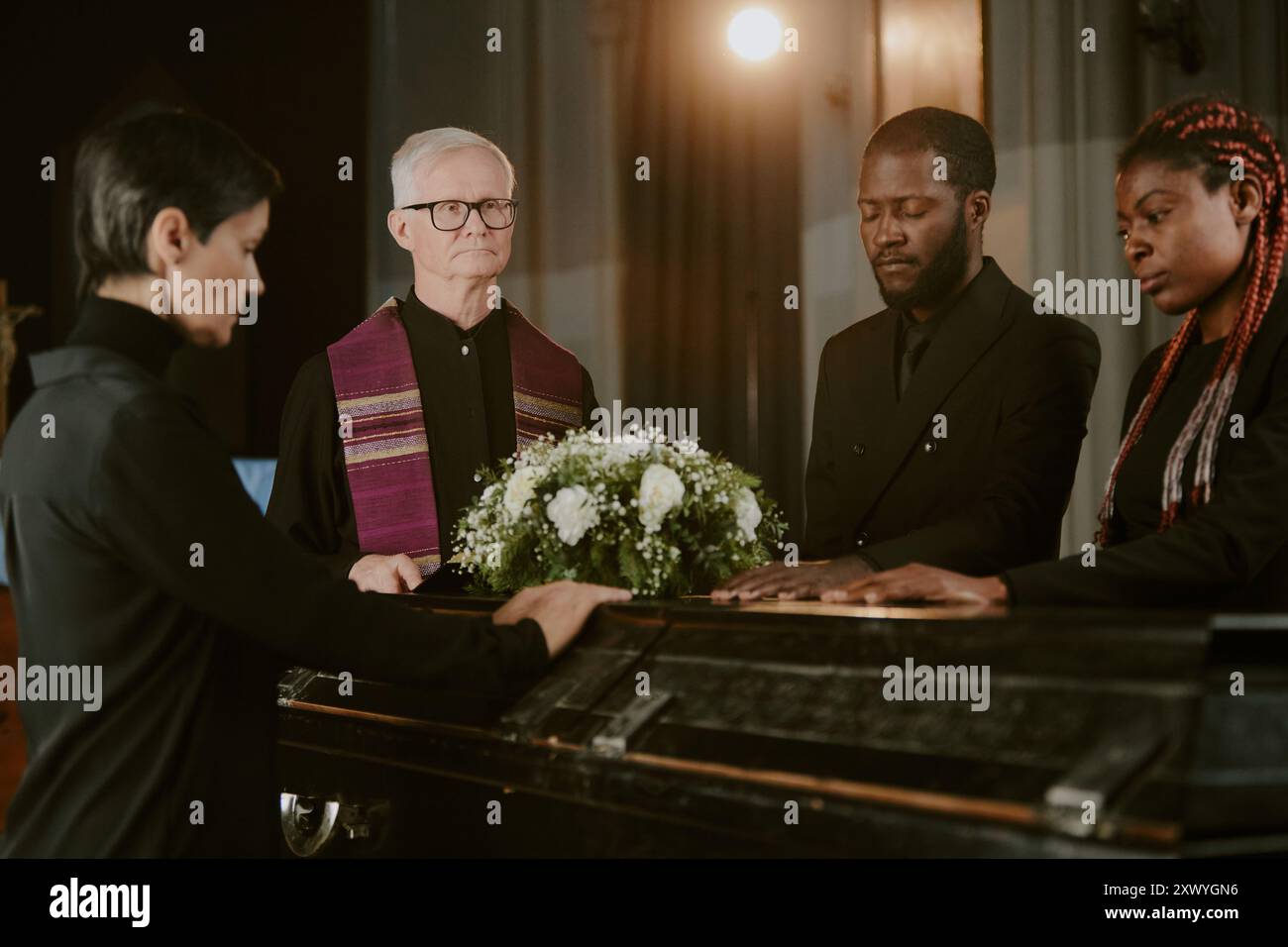 Black wooden coffin between biracial people who touching it in church ...