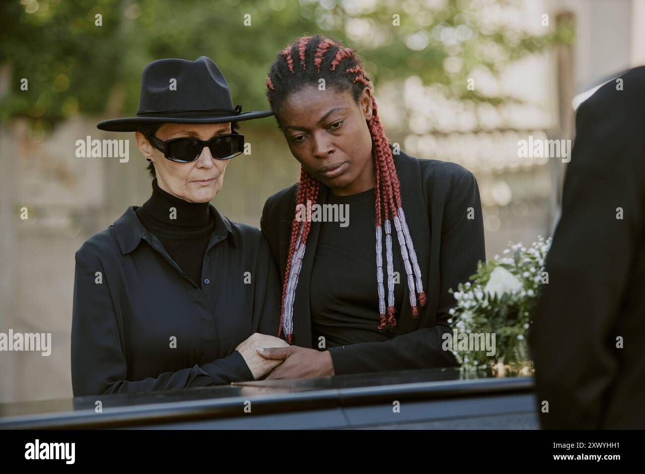 African American daughter supporting her caucasian mourning mom while ...