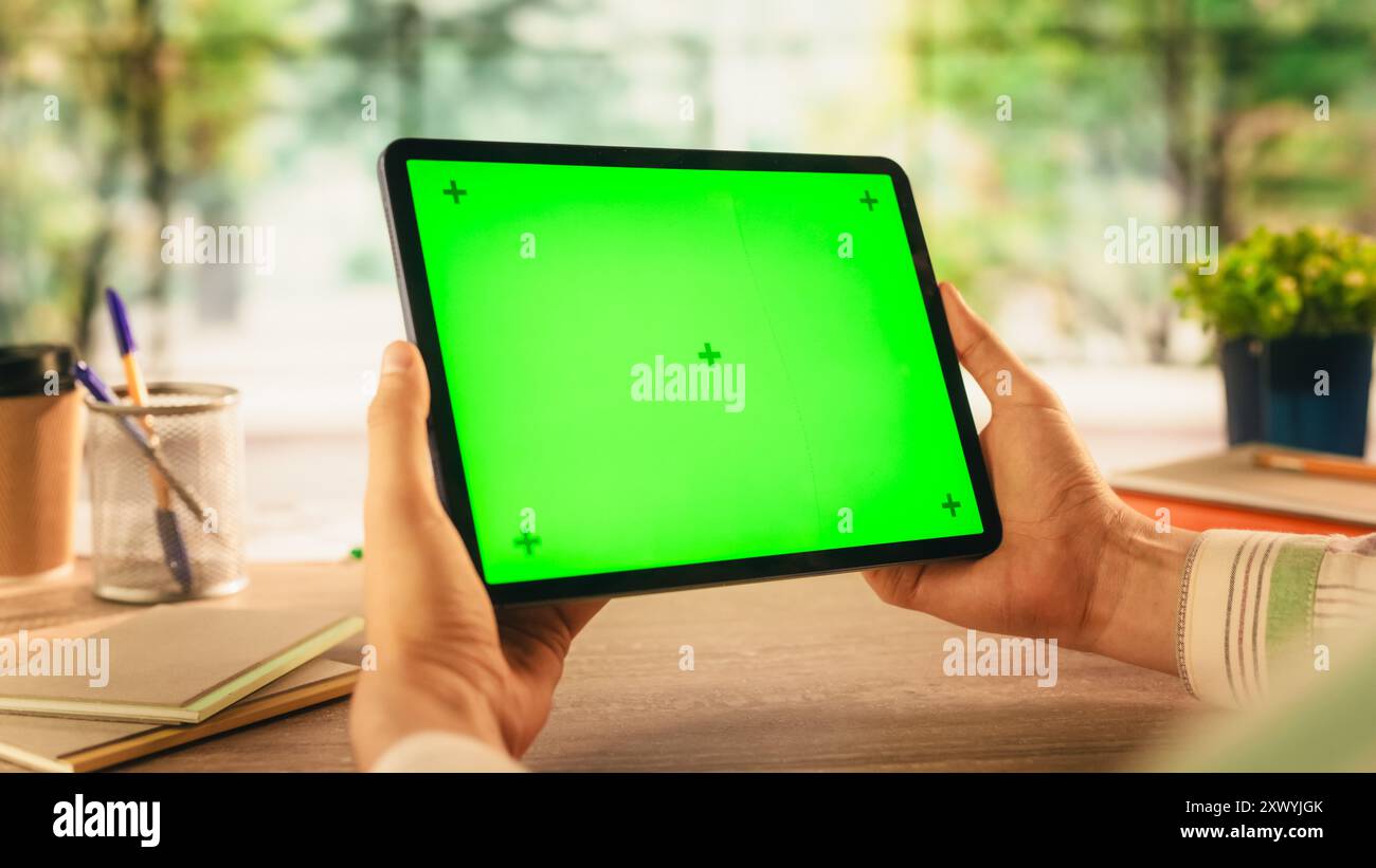 Anonymous Man Holding Tablet Computer with Green Screen Mock Up Display, Sitting Behind a Wooden ...