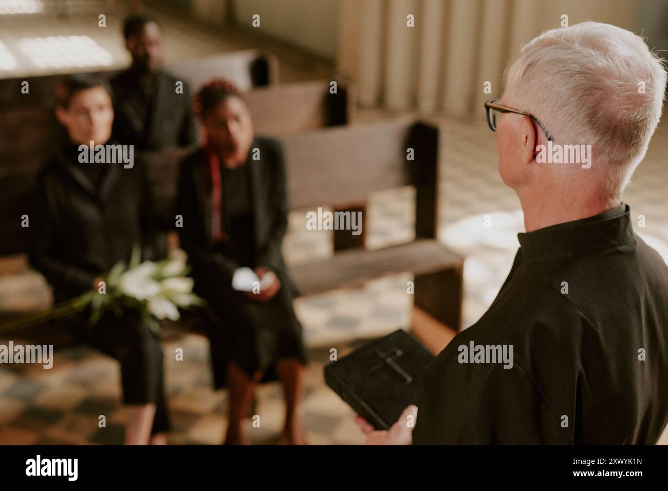 Over shoulder view of silver-haired priest offering up praying and ...