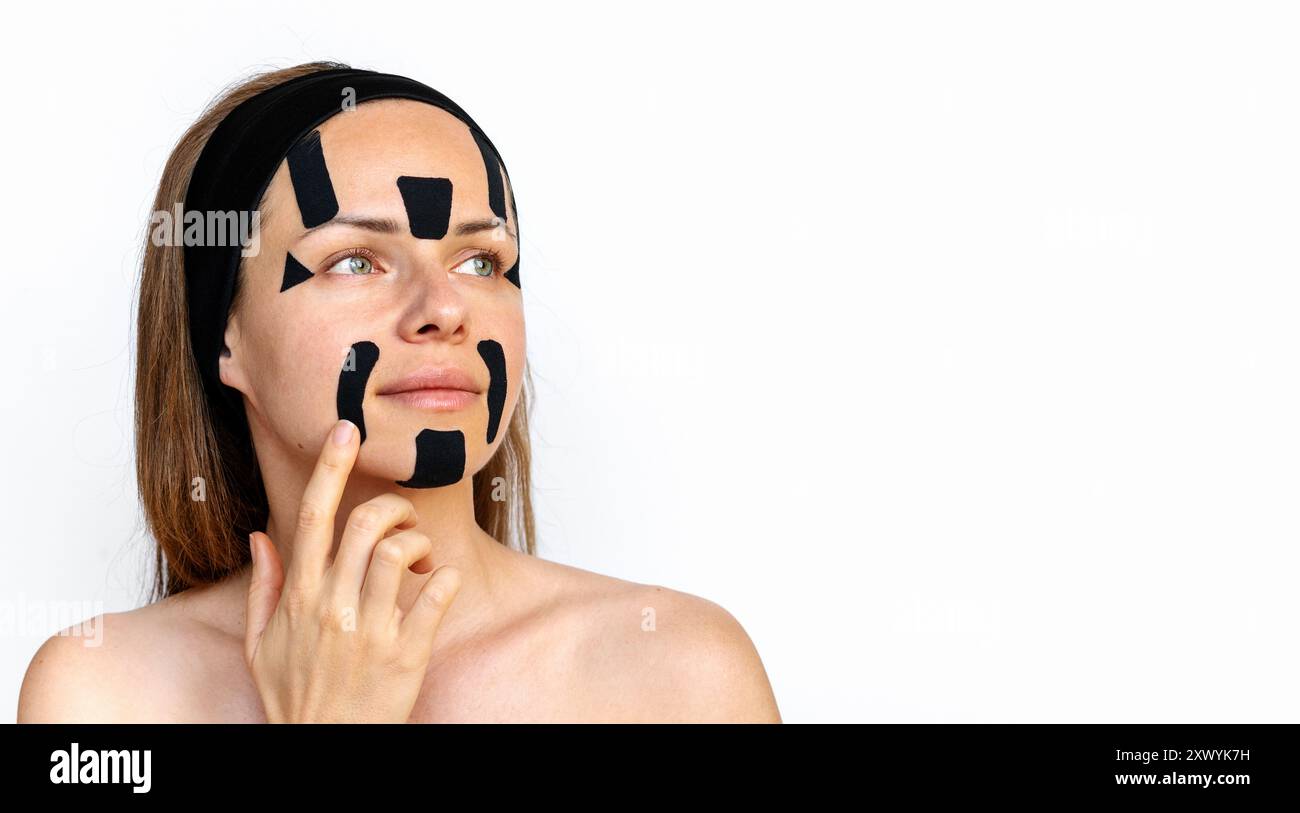 Young woman beauty model applies black colored facial tapes on her face ...