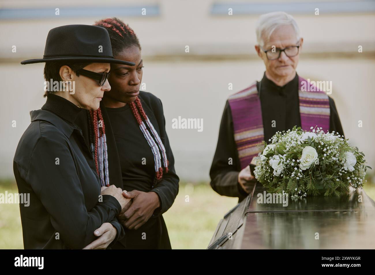 Gray-haired pastor reading prayer while mother and daughter bemoaning ...