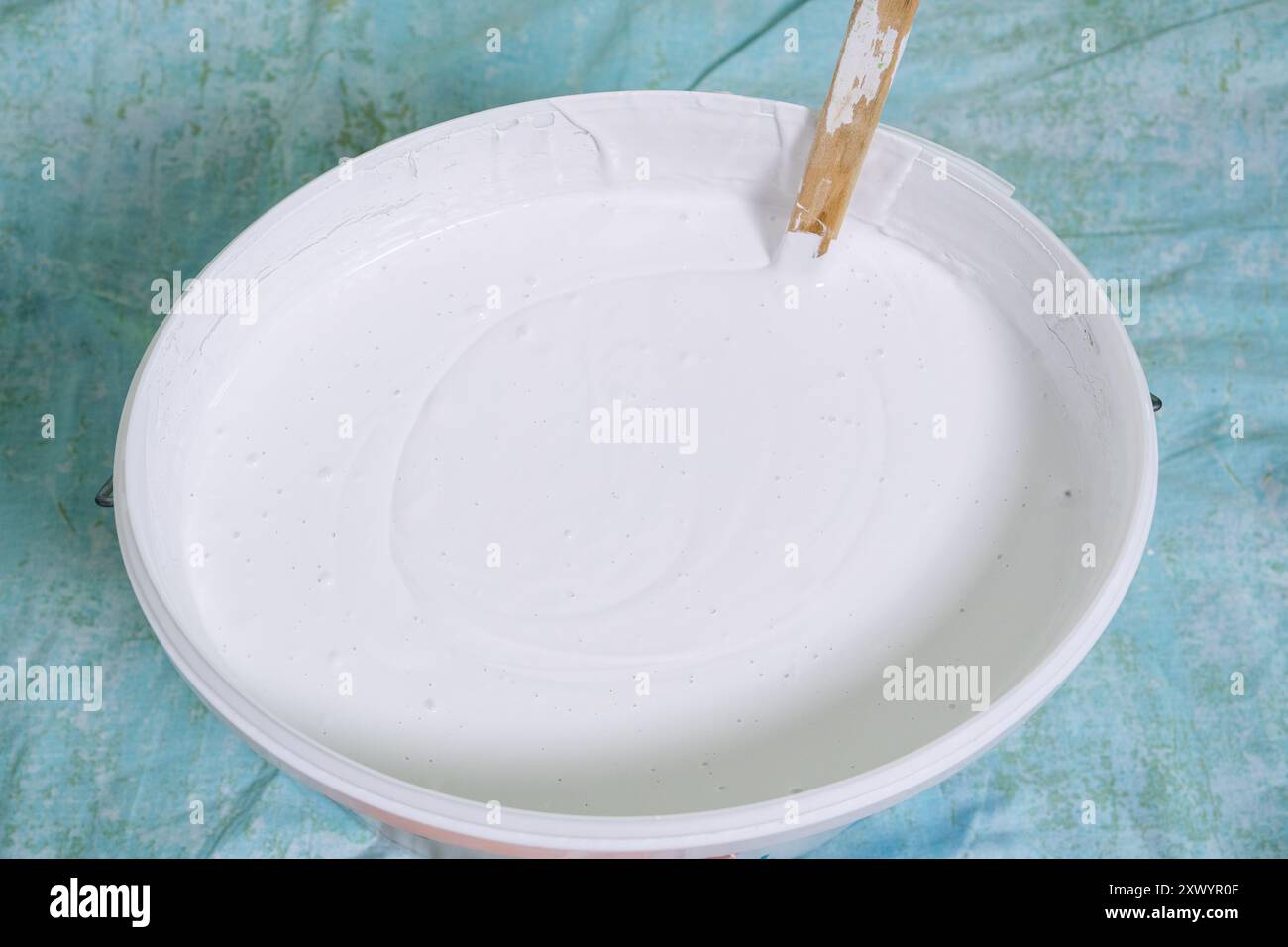 A bucket of white paint and brushes for mixing paint are on floor in ...