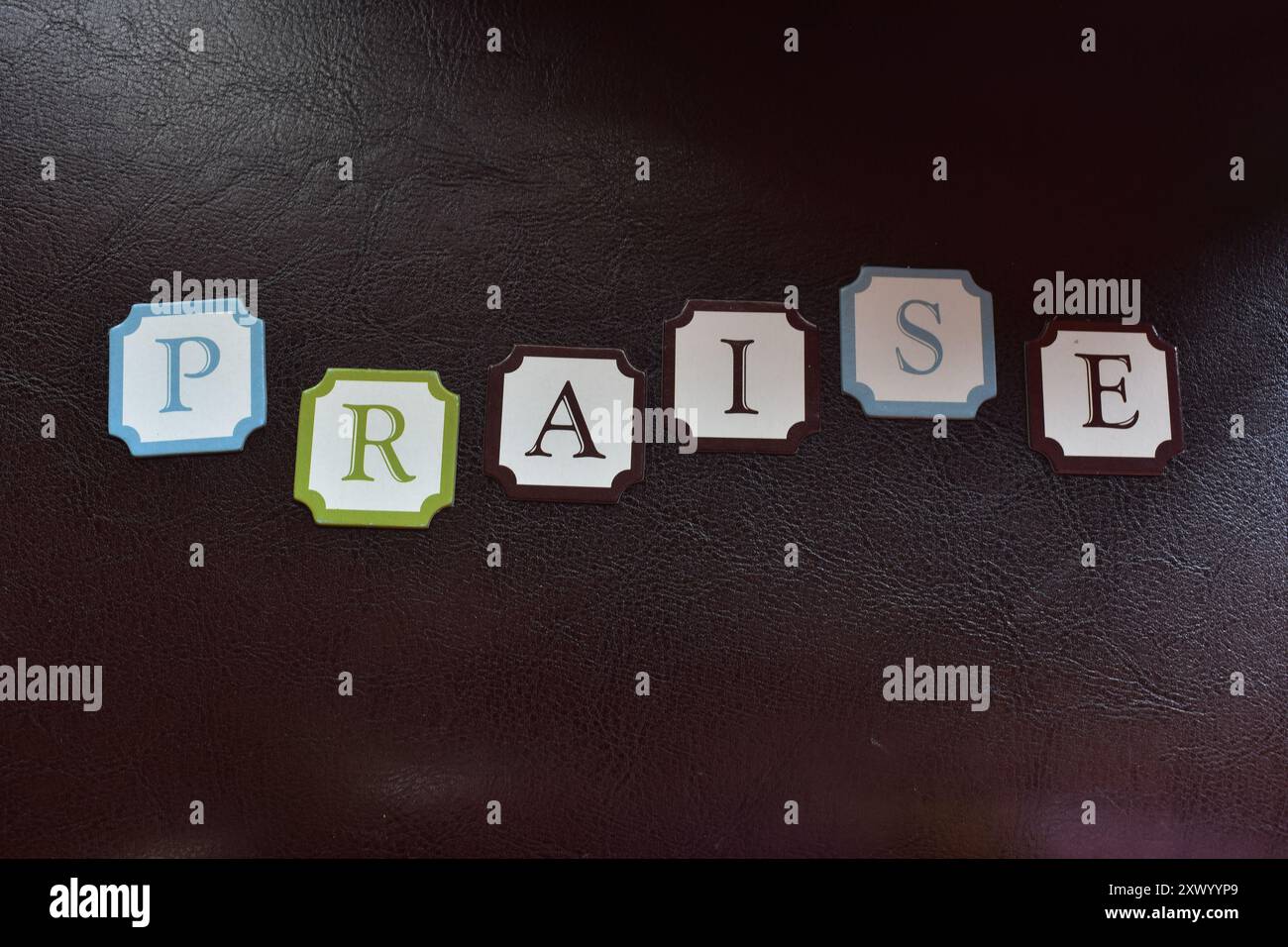 The word PRAISE formed with block style letters on a dark, textured ...