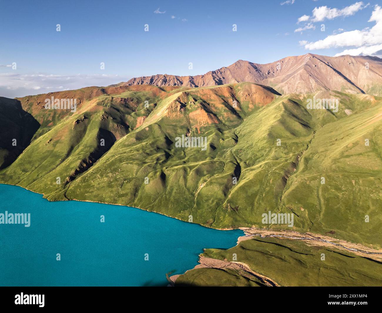 Aerial view of Kol Ukok Lake surrounded by green mountains under a blue ...
