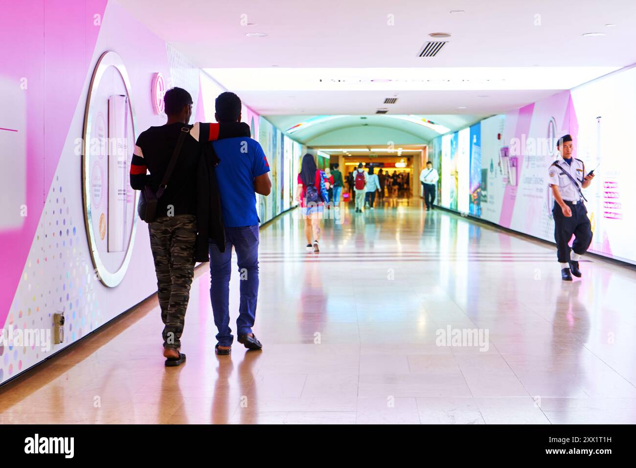 People walk along a long underground corridor with colored neon lights ...