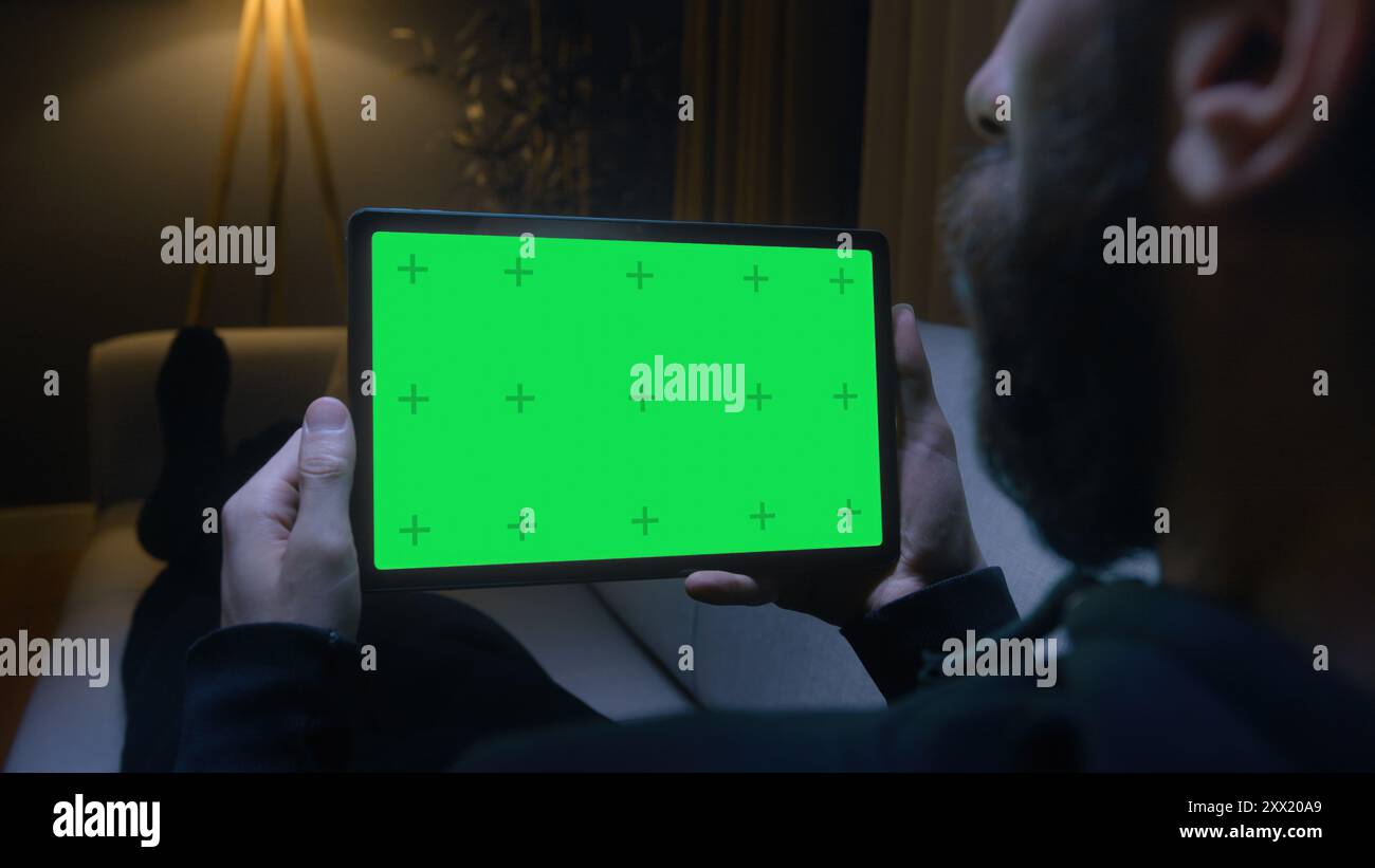 Man lying on couch using tablet horizontally with chroma key green screen, tapping, scrolling ...