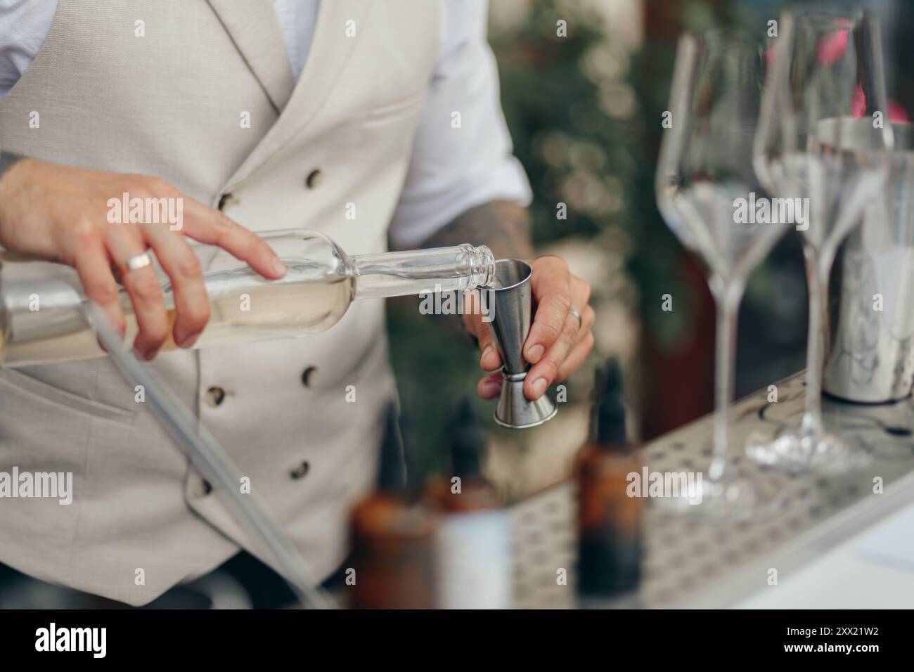 Bartender making a cocktail, pouring vodka from a bottle into a cocktail measuring cup, adding ...
