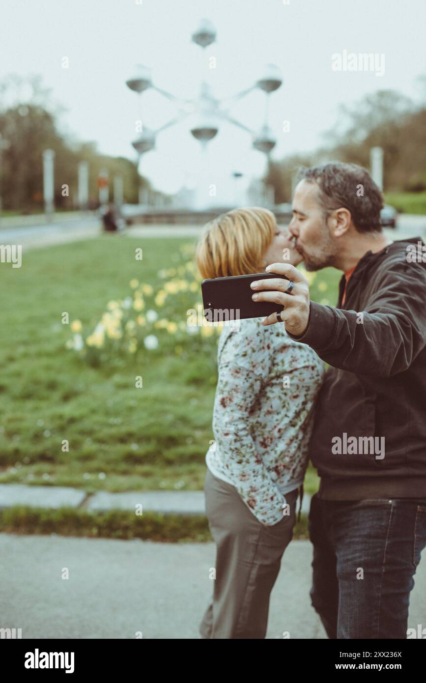 Kissing Couple taking a selfie in a park with the Atomium in the ...