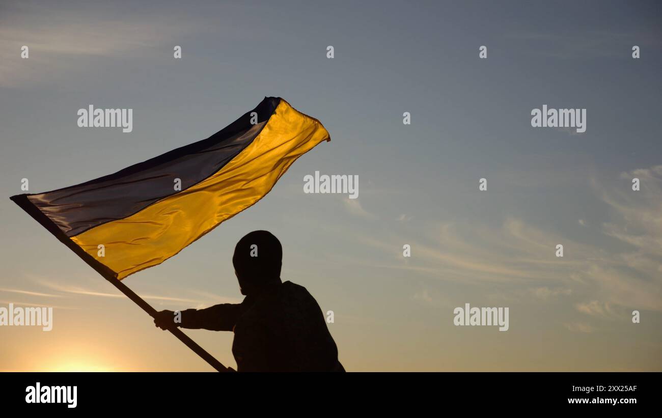 Young man in military uniform waving flag of Ukraine against beautiful ...