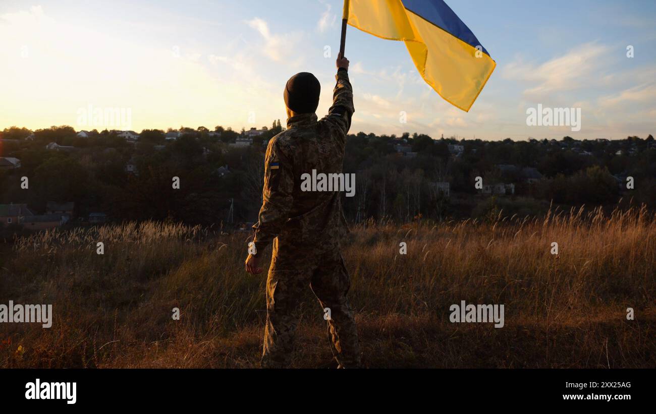 Male soldier stands with raised flag of Ukraine against background of ...