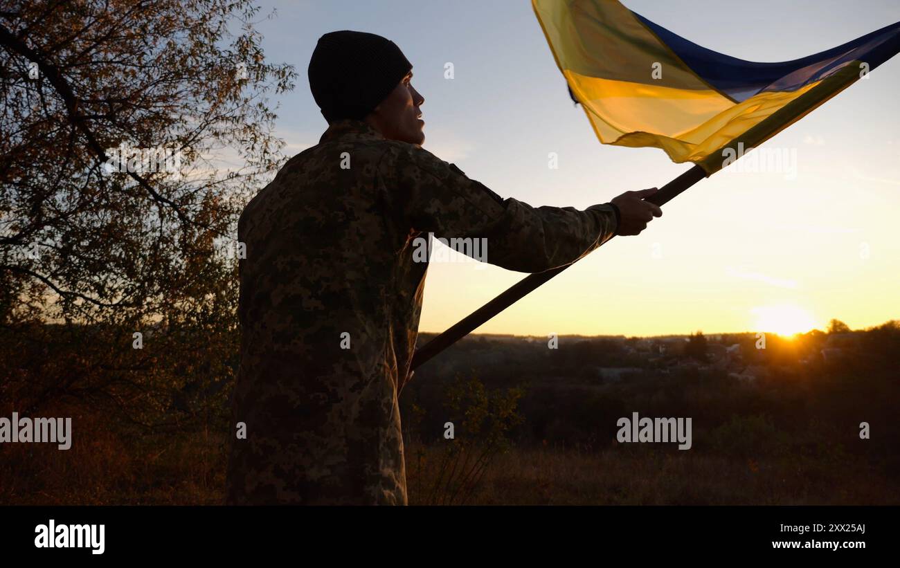 Young man in military uniform waving flag of Ukraine against beautiful ...