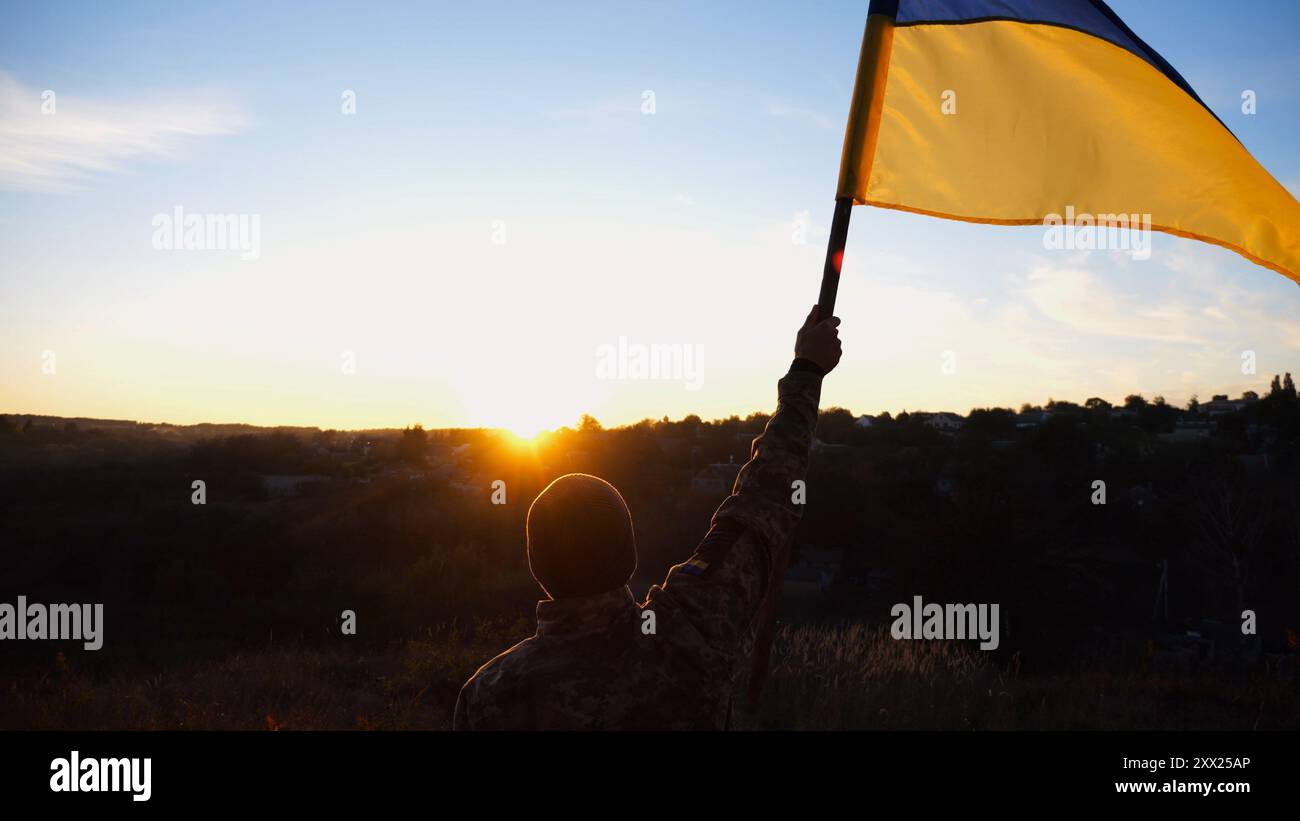 Male soldier stands with raised flag of Ukraine against background of ...